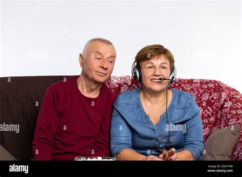 The Older Woman Communicates Online Using Large Headphones And A Microphone The Spouse Is