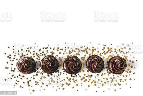 초콜릿 아이싱과 골드 스파클이 있는 골드 컵케이크는 황금별 모양의 색종이가 있는 흰색 배경에 반짝입니다 휴일 개념 디자인의