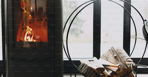 불타는 불이 있고 금속에 장작이 있는 현대적인 검은 벽난로는 산의 전망을 감상할 수 있는 커다란 창문을 배경으로 서 있습니다 추운 계절에 아늑하고 따뜻하고 차분한 순간