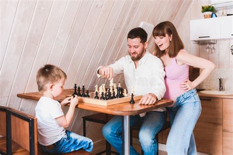 Pregnant Mom Watching Dad And Son Play Chess At The Table Stock Photo