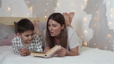 La Maman Lit Un Livre Son Fils Se Trouvant Sur Un Lit Dans Des Pyjamas Et L Embrasse Clips
