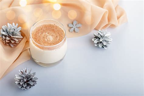계란 알코올 강판 육두구와 계피 클로즈업 복사 공간을 가진 전통적인 크리스마스 칵테일 Eggnog 베이지 색 장식 불타는 등불과 소나무 콘이있는 회색 테이블에 달콤한 전통