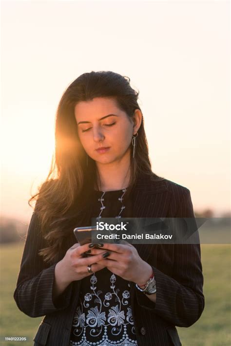 예쁜 히스패닉 소녀 미소와 석양에 그녀의 전화에 채팅 솔로 여행자 소셜 미디어 한 젊은 여자 관광 스마트 폰을 사용 하 여 즐거움 일몰 빛 초상화 다시 조명 여행 탐사 관광