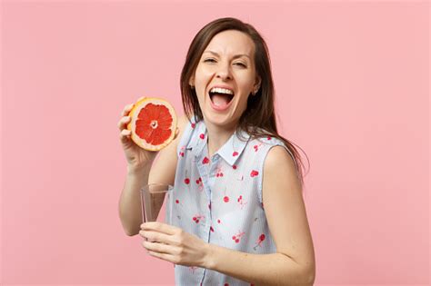 미친 분홍색 파스텔 벽 배경에 고립 된 신선한 잘 익은 자 몽 유리 컵의 절반을 들고 여름 옷에 젊은 여자를 웃 고 사람들은