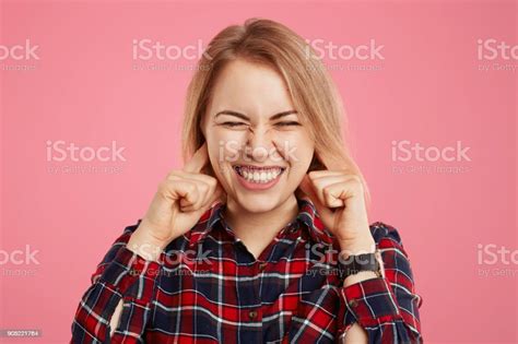 예쁜 여자의 스튜디오 샷 Clenches 치아와 불만으로 불쾌 한 사운드 나 음악을 듣는 귀를 플러그 매력적인 모습 분홍색