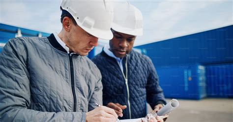 두 명의 엔지니어가 대형 상업용 화물 부두에서 선적 컨테이너 옆에 서서 클립보드의 재고 목록을 논의하고 있습니다 사진 Unsplash의 청사진 이미지