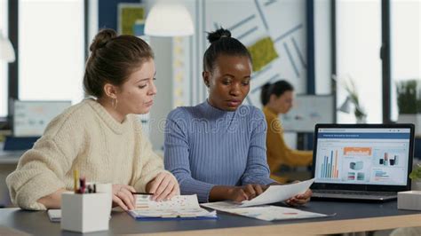 Team Of Colleagues Analzying Market Share Looking At Laptop Comparing Sales Charts On Clipboard