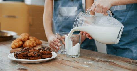 파란색 요리사 유니폼을 입은 두 명의 어린 소녀가 테이블에 쿠키가 있는 부엌의 안경에 우유를 붓는 모습을 클로즈업합니다 사진 Unsplash의 우유 이미지