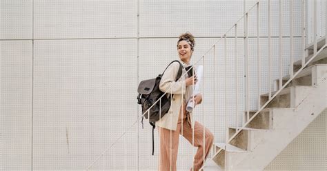 한 여성 젊은 성인 백인 여학생이 배낭을 메고 대학 건물 앞에 서서 종이와 커피 한 잔을 들고 밝은 날에 야외에서 행복한 미소를 지으며 실제 사람들이 공간을 복사한다 사진