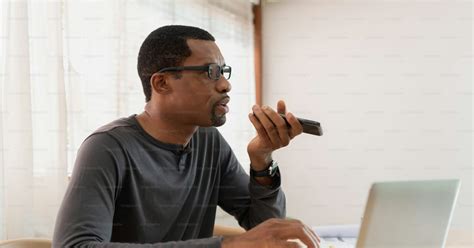 심각한 아프리카계 미국인 남성 프리랜서는 음성 인식을 사용하여 스마트폰을 말하고 직장에서 노트북 컴퓨터로 작업합니다 사진 Unsplash의 브라질 민족 이미지