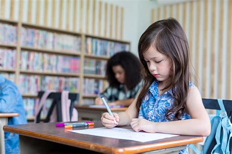 소녀는 교실에서 숙제를하고 있습니다 학교로 돌아 가기 귀여운 근면한 아이들이 실내의 책상에 앉아 있습니다 아이들은 수업에서 배우고 있습니다 아이에 대한 스톡 사진 및 기타