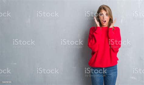 아름 다운 젊은 여자 겨울 스웨터를 입고 그런 지 회색 벽을 통해 서 깜짝 얼굴로 충격 무서 워 두려워 하 고 공포 식으로 흥분 감정에 대한 스톡 사진 및 기타 이미지