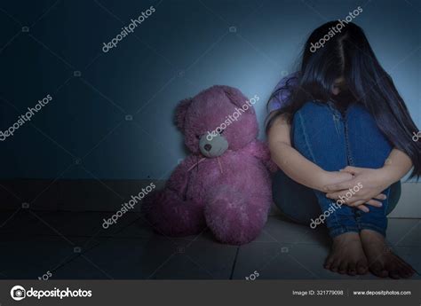 Грустная женщина обнимает колено и плачет сидя с плюшевым мишкой в темноте стоковое фото