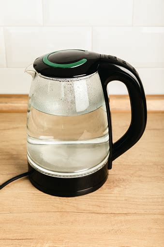주방의 나무 테이블에 있는 현대적인 전기 투명 주전자 물을 끓이고 차를 만들기위한 주전자 뜨거운 음료를 만들기위한 가전 제품 복사 공간 텍스트를 위한 장소입니다 가정 주방에