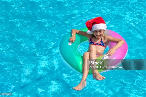 산타 클로스 모자를 쓰고 있는 아이가 화창한 화창한 날에 푸른 수영장에서 수영하고 미소짓고 있습니다 새해 복 많이 받으세요 와 크리스마스의 개념입니다 텍스트를 위한 공간
