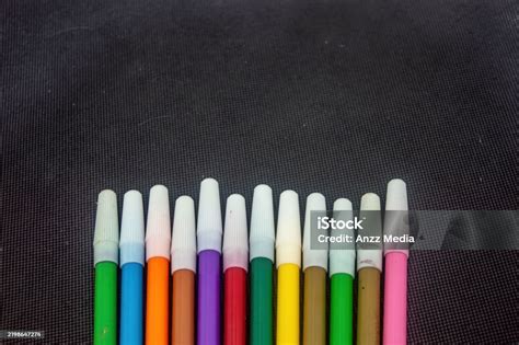어두운 질감의 표면에 깔끔하게 배열된 흰색 캡이 있는 다채로운 마커 행 생생한 색상과 질서 정연한 배열은 시각적으로 매력적이며 예술 및 공예 프로젝트에 유용합니다 공예에