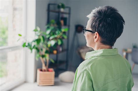 늙은 여자가 카키색 셔츠를 입고 편안한 깊은 생각을 하고 창문을 보고 중요한 결정을 내리고 사무실에서 고립된 평온함을 느끼는 뒷모습 중장년에 대한 스톡 사진 및 기타 이미지