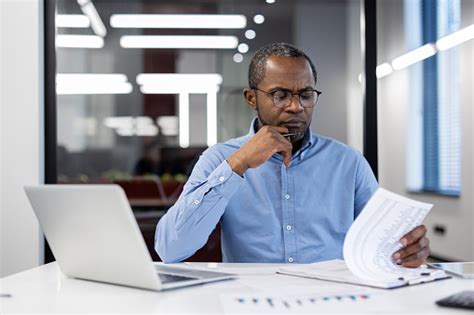 노트북과 사려 깊은 표현으로 현대적인 사무실 환경에서 재무 문서를 분석하는 성숙한 사업가 검사 보기에 대한 스톡 사진 및 기타 이미지 검사 보기 결정 경영자 Istock