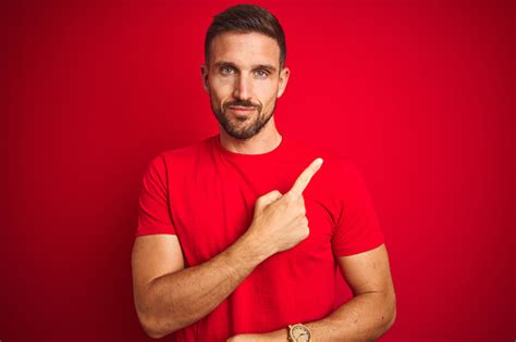 빨간 고립 된 배경 위에 캐주얼 티셔츠를 입고 젊은 잘 생긴 남자는 광고를 보여주는 측면에 손으로 손가락을 가리키는 심각하고 차분한 얼굴 T 셔츠에 대한 스톡 사진 및 기타