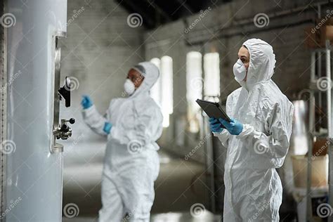 Two Female Supervisor In Hazmats Using Tablet Monitoring Fermentation