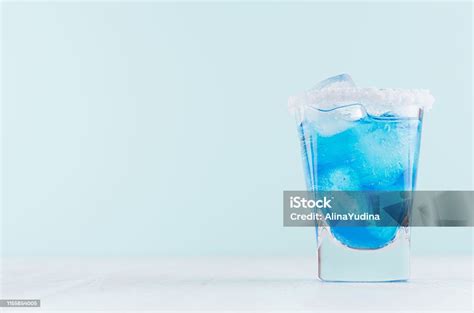블루 큐라소 리큐어 아이스 큐브 부드러운 밝은 흰색 파스텔 녹색 배경에 냉동 샷 유리소금 테두리와 열대 신선한 알코올 칵테일