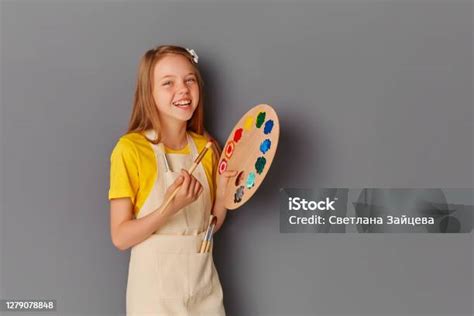 회색 벽에 나무 팔레트와 브러시를 들고 아름다운 젊은 십대 소녀의 초상화 예술 팔레트와 예술가의 브러시를 손에 들고 웃고 있는 아이 아이들의 창의력을 위한 아이템 아이에