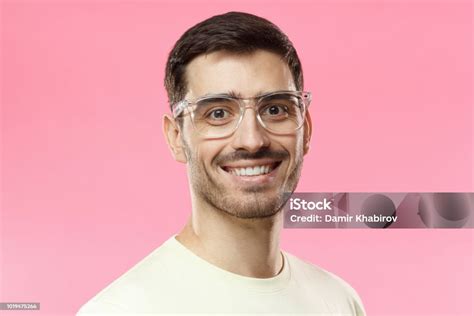핑크 바탕에 고립 된 젊은 잘생긴 백인 남자의 실내 얼굴만 입고 캐주얼 셔츠 유행 플라스틱 안경을 쓰고 진정 얼굴 표현과 행복 한 미소와 함께 카메라를 보고 T 셔츠에 대한