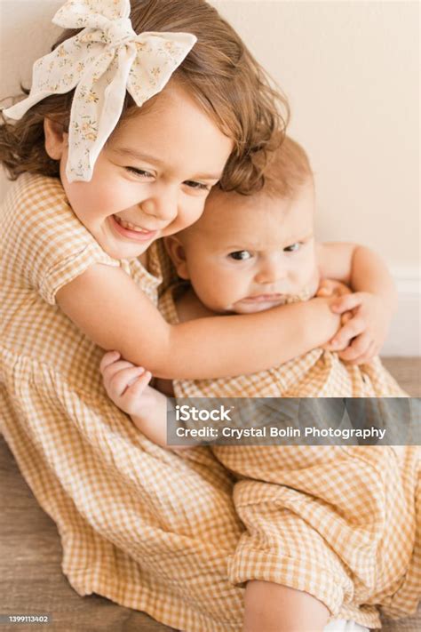 3 살짜리 유아 소녀가 약간 걱정하고 짜증을 내며 4 개월 된 아기 형제와 어울리는 노란색 격자 무늬 의상을 입고 함께 앉아있는 동안 2 5 개월에 대한 스톡 사진 및 기타