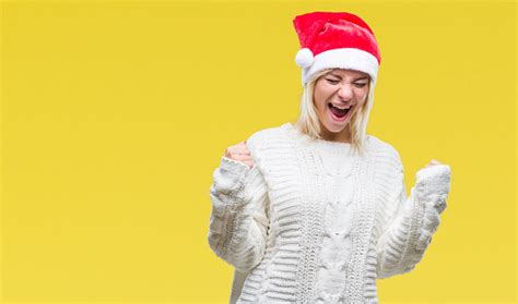 젊은 아름 다운 금발 여자 매우 행복 하 고 흥분 무기와 우승자 제스처를 하 고 격리 된 배경 위에 크리스마스 모자를 쓰고 웃 고 성공을 위한 비명 축 하 개념입니다 겨울에