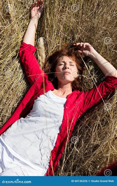 женщина 50s наслаждаясь спать тепла солнца один на сухой траве Стоковое Фото изображение