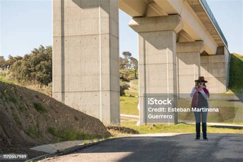 모자를 쓴 한 여성이 그리말도 근처 기차 선로의 고가도로 아래에서 스마트폰으로 사진을 찍고 있다 건축에 대한 스톡 사진 및 기타 이미지 Istock