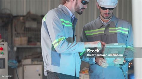 안전 유니폼을 입은 전문 엔지니어 원격 컨트롤러를 사용하여 로봇 팔을 용접 공작물로 제어하여 산업 제조 공장의 사양을 충족합니다 기술자 팀이 용접 화재 중 자동화 로봇