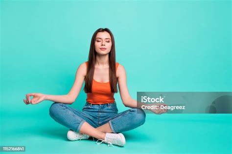 전체 길이 몸 크기 사진 아름 다운 그녀의 그녀의 여자 주말 앉아 바닥 교차 다리 로터스 포즈 눈 폐쇄 명상 착용 캐주얼 오렌지 탱크 탑 청바지 데님 고립 된 밝은 청록