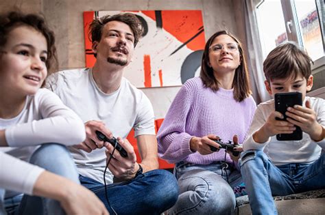 집에서 소파에 앉아 조이스틱으로 비디오 게임을 하는 아이들과 함께 있는 어머니와 아버지 10 11세에 대한 스톡 사진 및 기타 이미지 10 11세 25 29세 4 5