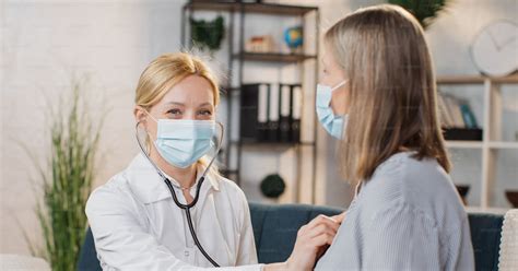 전문가는 안면 마스크를 착용하고 노인 여성 환자를 검사하고 가정 방문 및 검진 중에 청진기를 사용하여 청진기를 사용하는 유쾌한