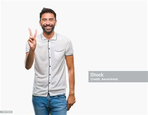 승리 표시를 하 고 카메라에 윙크 하는 행복 한 얼굴로 웃 고 고립 된 배경 위에 성인 히스패닉 남자 번호 2입니다 긍정적인 감정 표현에 대한 스톡 사진 및 기타 이미지