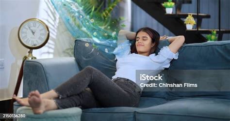 행복한 Z 세대 아름다운 미소 짓는 여성은 소파에 앉아서 휴식을 취하고 팔을 들어 올리고 근육을 다시 뻗고 집에서 평화로운 주말을 즐깁니다 인도 Gen Z 게으른 여성은