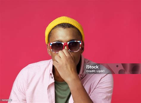 핑크색 셔츠를 입은 젊은 잘 생긴 아프리카 계 미국인 남자와 영국 붉은 배경에 고립 된 영국 국기 선글라스를 코를 덮고있는 나쁜 냄새의 몸짓 30 34세에 대한 스톡 사진