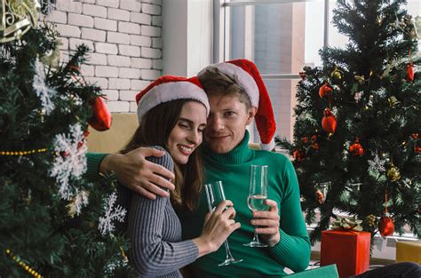 빨간 산타 모자와 젊은 커플 남자는 샴페인을 마시고 집 휴일 가족 새해 복 야 및 메리 크리스마스 축제 개념에서 축하 크리스마스 트리와 그의 여자 친구를 키스 즐길 수