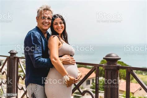 여름 방학 동안 아름다운 바다 풍경에 서있는 임신 한 여성과 행복한 부부 젊은 아내와 남편은 아기를 기대하며 함께 웃고 있습니다 임신 가족 및 사랑 개념 2명에 대한 스톡