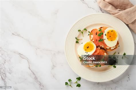 맛있는 토핑 훈제 연어 계란 허브 마이크로 그린 무 흰색 대리석 테이블 배경에 흰색 접시 위에 검은 참깨를 샌드위치 건강한 오픈