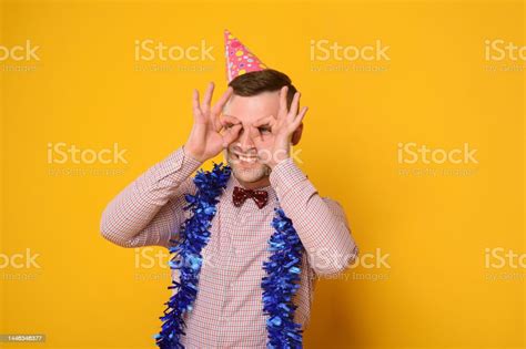 파티 모자를 쓴 남자는 손에서 안경을 만들고 노란색 배경에 미소를 짓는다 공휴일에 대한 스톡 사진 및 기타 이미지 공휴일 긍정적인 감정 표현 나비 넥타이 Istock