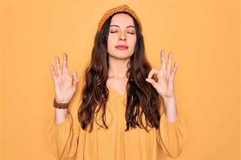 노란색 배경 위에 서있는 캐주얼 티셔츠와 Diadem을 입은 젊은 아름다운 여성은 손가락으로 명상 제스처를하고 눈을 감고 미소 요가 개념입니다 T 셔츠에 대한 스톡 사진 및