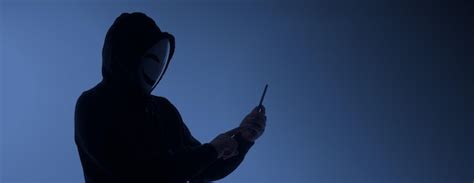Premium Photo Hacker Anonymous And Face Mask With Smartphone In Hand