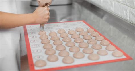 실리콘 매트에 마카롱 반죽을 바르는 과정 베이킹 실리콘 매트에 갈색 아몬드 반죽을 짜내고 페이스트리 백을 들고 있는 여성의
