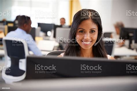 바쁜 사무실에서 헤드셋과 컴퓨터에서 일 하는 젊은 여자 사무실에 대한 스톡 사진 및 기타 이미지 사무실 영국 일함