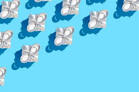 파스텔 블루 배경에 은색 활이 있는 반짝이는 흰색 선물 상자로 만든 창의적인 패턴 크리스마스 또는 생일 선물 개념입니다 휴일 테마 최소한의 스타일 2023년에 대한 스톡