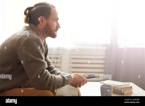 Side View Portrait Of Modern Bearded Man Watching Tv At Home And