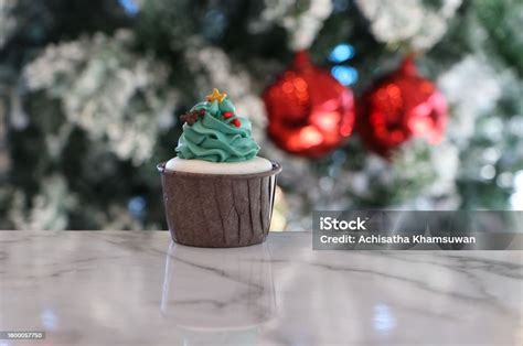 녹색 버터 크림으로 장식 된 컵 케이크 갈색 컵에 금색 별이 있는 크리스마스 트리 패턴입니다 흰 눈과 두 개의 빨간 공이 있는 크리스마스 트리의 초점이 맞지 않는 배경에