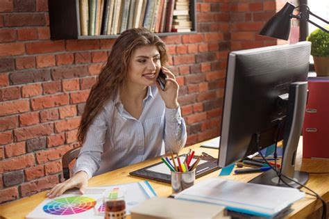 집에서 또는 로프트 스타일 사무실에서 작업 긴 머리를 가진 젊은 여성 그녀는 스마트 폰을 통해 말하기와 미소 디자이너 편집자 일러스트레이터 또는 디지털 아티스트 직업
